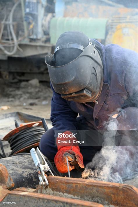건설 현장에서 금속 부품을 용접하는 작업자 용접공이 노천 탄광에서 대형 기계의 부품을 용접합니다 수동 작업의 흥미로운 예입니다