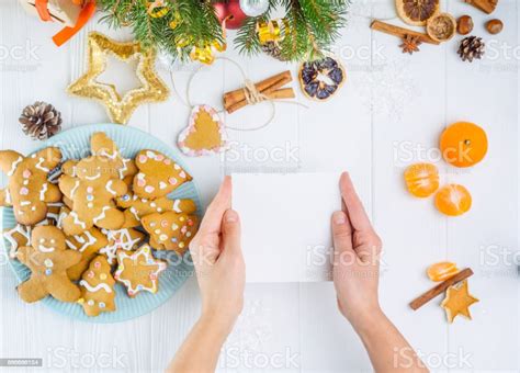 상위 뷰 여성 손에 들고 Gingerbred 쿠키와 하얀 나무 테이블 아래에서 빈 인사말 카드 크리스마스 트리 장식 향신료와