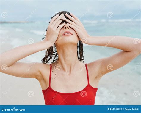 Woman In Red Swimsuit On Ocean Beach With Wet Hair Covers Face With