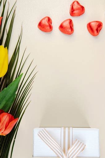 빨간 호일 선물 상자 및 복사 공간이 있는 흰색 배경에 다채로운 튤립 꽃다발로 싸인 하트 모양의 초콜릿 사탕의 평면도 0명에