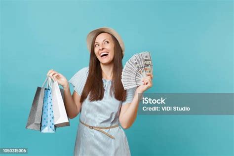 여름 복장 쇼핑 후 구매와 패키지 가방을 들고 밀 짚 모자에에서 세로 젊은 여자 많은 달러 지폐 현금 돈 파란색 배경에 고립 광고에 대 한 공간을 복사 합니다 가방에 대한