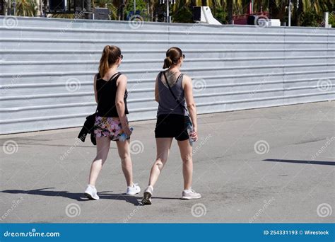 Two Young Men With Their Hair Tied Back Walk Together With Bottles Of