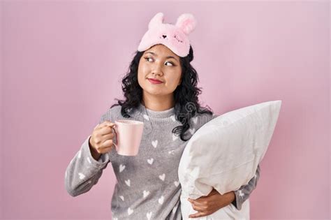 Young Asian Woman Wearing Sleep Mask And Pajama Hugging Pillow Drinking