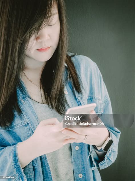 아시아 Hipster 소녀 동안 블루 자 켓 진 누른 소프트 포커스 배경으로 그녀의 스마트폰에서 이메일 및 그녀의 쇼핑 목록 확인 개인 장식품에 대한 스톡 사진 및 기타