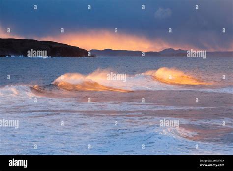 Large Waves Crash In A Winter Storm And The Swirling Spray Is Illuminated By The Warm Light Of