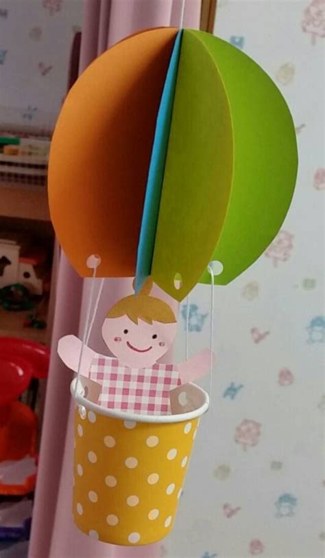 カラフルなドット柄の紙コップ（オレンジ・赤・水色）の気球に子どもが乗っています。 全部で12個作りました。 少しの風で気球がクルクル回りますよ