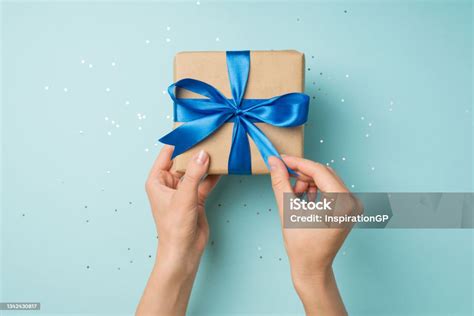 고립된 파스텔 블루 배경에 반짝이는 스팽글 위에 선명한 파란색 사틴 리본 리본 리본이 달린 수제 종이 기프트박스 1인칭 탑 뷰