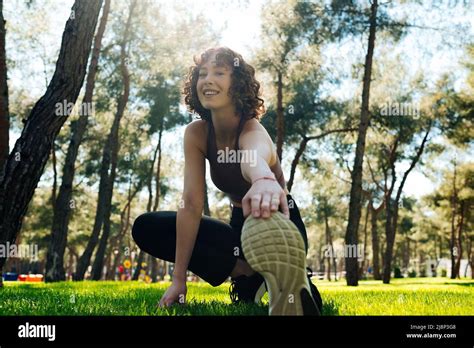 Redhead Woman Wearing Sports Bra And Black Yoga Pants Stretching Exercises And Smiling While