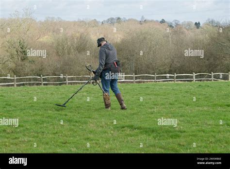 A Metal Detectorist In A Field Searching For Metal Objects Hidden In