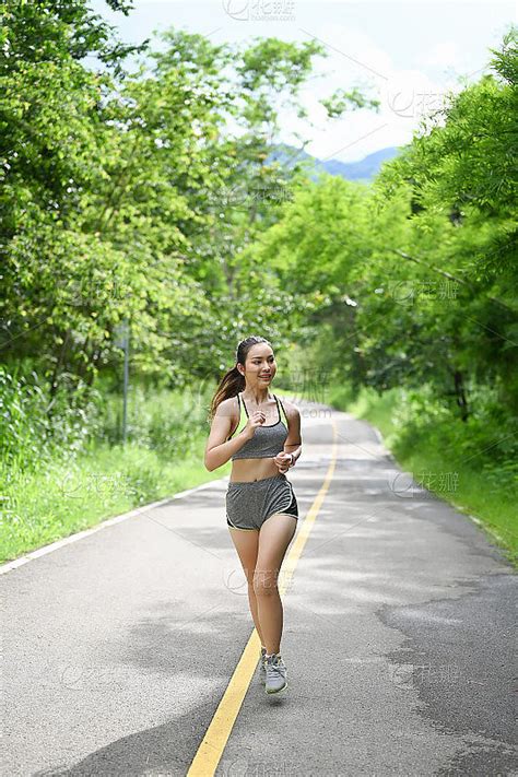 一个穿着运动服的漂亮女人在以自然为背景的道路上慢跑。