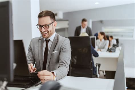 고도로 동기 부여 된 남성 코 카 서 스는 자신의 직장에 앉아서 컴퓨터를 사용 하 여 남자 직원을 웃는 미소 배경에 그의 동료 작업 경영자에 대한 스톡 사진 및 기타 이미지