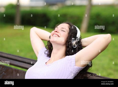 Happy Woman Resting Sitting On A Bench Listening To Music In A Park