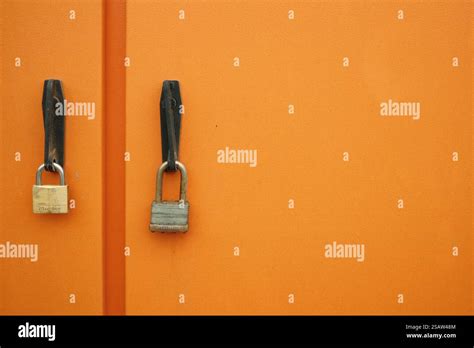 Two Padlocks Fastened On An Orange Metal Door Symbolizing Security Protection And Access