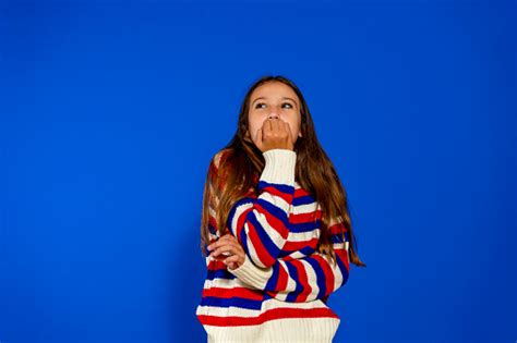 클로즈업 초상화 어린 소녀는 손가락 손톱을 물고 불안하고 고립 된 파란색 배경에 대한 두려움으로 당신을 바라보며 인간의 얼굴 표정 신체 언어 반응 삶의 지각 10 11세에