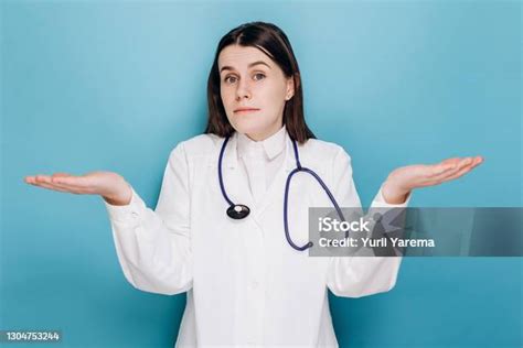 흰색 코트를 입은 우유부단한 여성 의사의 초상화가 흔들리고 고민하는 대답을 보고 파란색 벽에 고립되어 있는지 모른다