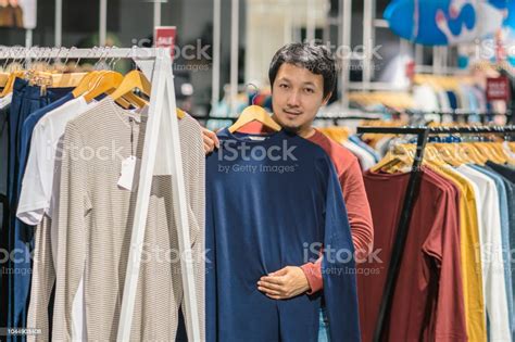 스마트 아시아 남자 쇼핑 센터에서 옷이 게에서 옷을 선택 하는 수염과 다채로운 Tsshirts 패션과 소비 개념을 찾고 개념에