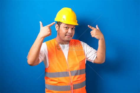 亚洲建筑工人穿着橙色安全背心和蓝色背景头盔高清图片下载 正版图片503862657 摄图网