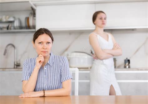 Angry Mother Sitting At The Kitchen Table And Offended Teenage Daughter