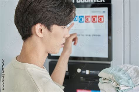 셀프 서비스 세탁실에서 빨래를 손에 올리고 키오스크를 작동중인 젊은 아시아 한국 남자 모델 Stock 写真 Adobe Stock