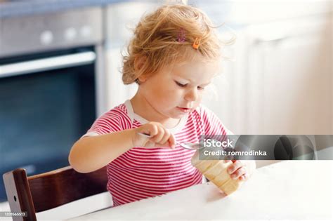와플 콘에 숟가락 달콤한 아이스크림에서 먹는 사랑스러운 아기 소녀 음식 어린이 수유 및 개발 개념 귀여운 유아 숟가락이 있는 딸이 의자에 앉아 서서 그 자체로 먹는 것을