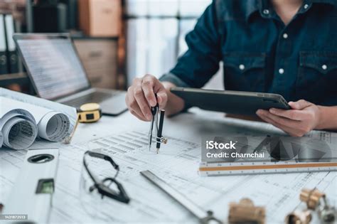 사무실 책상과 계산기 삼각형 눈금자 안전 안경 나침반 블루프린트의 버니어 캘리퍼에서 도면 검사 및 쓰기로 작업하는 엔지니어링 엔지니어 건축가 산업 및 공장 개념 공학에 대한