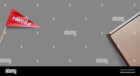 Small Paper Flags With The Warning Fragile As A Label And Empty Cardboard Box On Monochrome