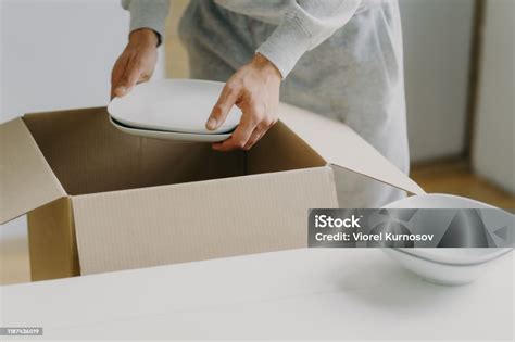 알 수없는 얼굴없는 바쁜 남자의 자른 이미지는 요리와 상자를 풀고 흰색 접시를 들고 새 아파트에서 움직이고 부엌에서 정리하고