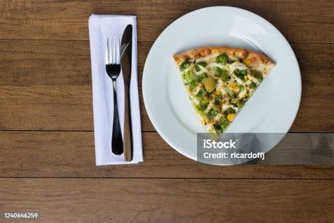 브로콜리 피자는 나무 판에 제공됩니다 모짜렐라 브로콜리 옥수수 완두콩 올리브로 구운 제품입니다 접시에 담긴 피자 조각 포크와 칼 수평 상단 사진입니다 길거리 음식에 대한