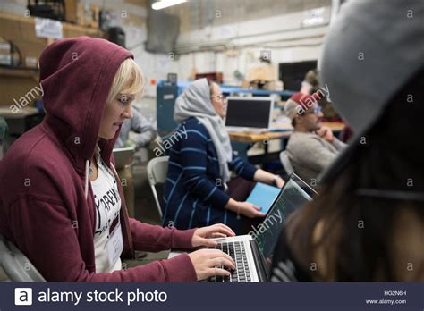 female hacker wearing hoody working hackathon at laptop in workshop
