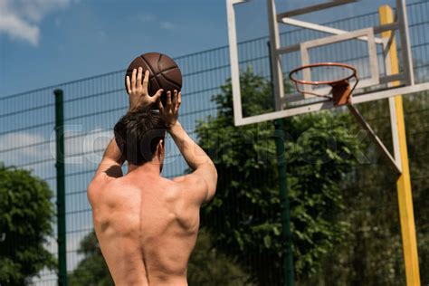 Back View Of Shirtless Basketball Player Throwing Ball In Basket At