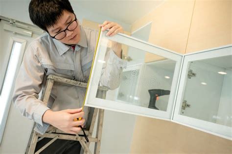 Asian Male Furniture Assembler Using Tape Measure On Cabinet Stock