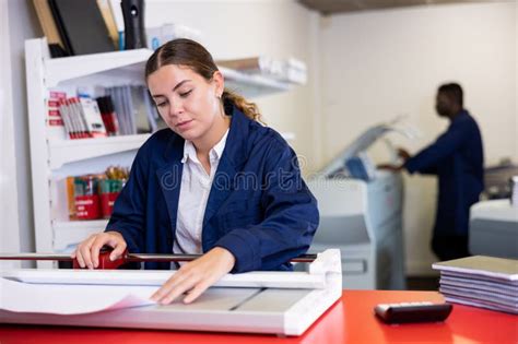 Positive Female Employee At Printing House Cuts Paper With Paper Cutter