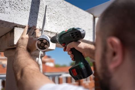 Premium Photo Man With A Drill Installing Security Cameras For
