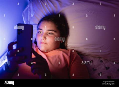 Serious Teenage Girl Looking At Screen While Lying On Bed In T Shirt In