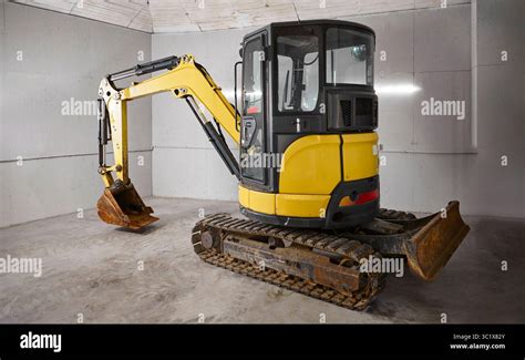 A Yellow Mini Excavator Sits On A Concrete Floor Inside A Gray Industrial Looking Room The