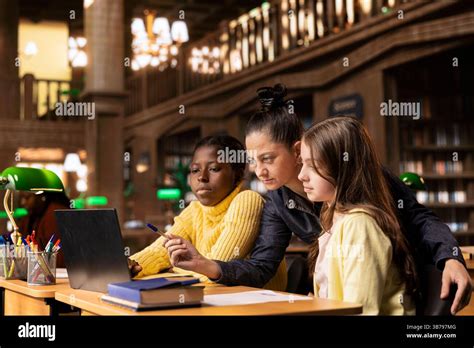 Caucasian Tutor Guiding Two Elementary School Girls At A Library Desk