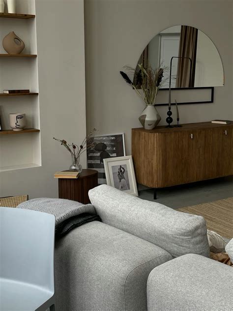 가구 배치 거실 거울 꽃병 나무 콘솔 러그 미니멀리스트 베개 베이지 소파 부드러운 색조 선반 세라믹 장식 스타일리시한 식물 아늑한 아트워크