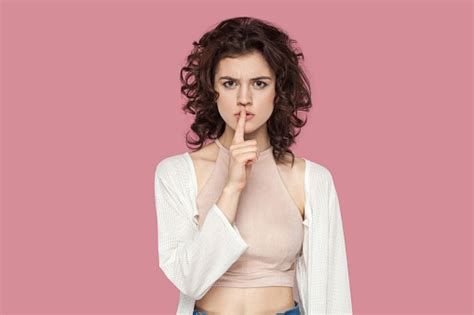 조용히 하세요 침묵 제스처와 입술에 손가락으로 서 캐주얼 스타일에 곱슬 헤어스타일으로 심각한 아름 다운 갈색 머리 젊은 여자의 초상화 손가락을 입술에 대기에 대한 스톡 사진
