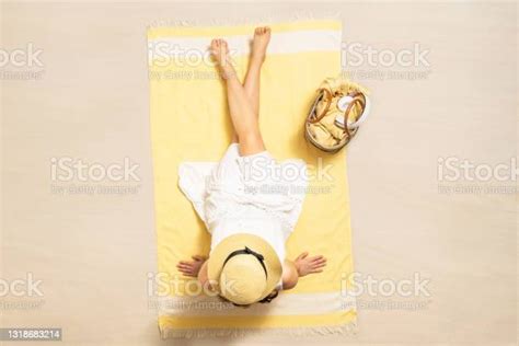 밀짚 모자를 쓰고 가방과 헤드폰이 달린 노란 비치 타월에 앉아 있는 드레스를 입은 여성 여름 방학에 해변의 모래에 여성 휴식