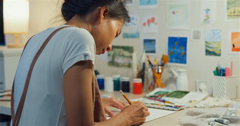 청소년 아시아 숙녀는 앞치마를 입고 책상 앞에 앉아 스케치북에 그림을 그리며 밤에는 집에서 아늑한 작업장으로 예술 작품을 만듭니다 현대 화가 추상 현대 미술 창의성 및