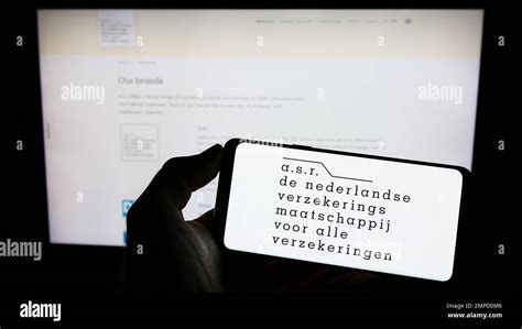 Person Holding Mobile Phone With Logo Of Dutch Insurance Company Asr
