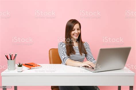 파스텔 핑크 배경에 고립 된 Pc 노트북으로 사무실에 앉아 하는 동안 프로젝트에서 작업 하는 캐주얼 옷에 젊은 웃는 여자 성과 비즈니스 경력 개념입니다 광고에 대 한 공간을