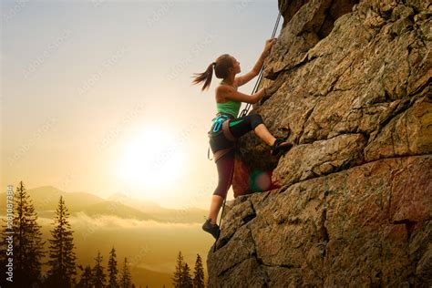 Beautiful Woman Climbing On The Rock At Foggy Sunset In The Mountains