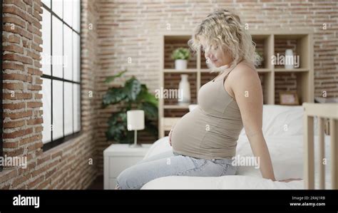 Young Pregnant Woman Touching Belly Sitting On Bed At Bedroom Stock