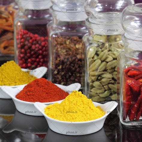 عکس ادویه ها و گیاهان متفاوت در ظرف های شیشه ای و کاسه های سفید در پس
