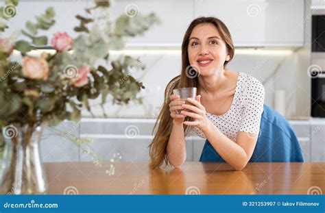 Smiling Middle Aged Woman Drinking Cappuccino Leaning On Kitchen Table