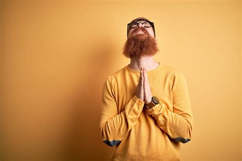 노란색 고립 된 배경에 안경을 쓰고 있는 잘 생긴 아일랜드 빨간 머리 남자는 매우 감정적이고 걱정되는 얼굴에 희망 표현과 함께 손을 구걸하고기도합니다 구걸 감정에 대한 스톡