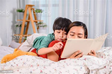 아시아의 어머니는 아들과 함께 집으로 일합니다 엄마와 아이는 침대에서 잠들기 전에 동화를 읽는다 여성의 라이프 스타일과 가족
