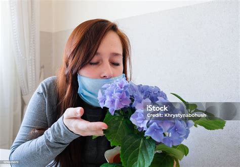 悲傷的婦女穿著醫療防護面罩在家隔離女孩嗅著藍色的繡球花大流行情緒 照片檔及更多 2019冠狀病毒病 照片 2019冠狀病毒病 人 位置