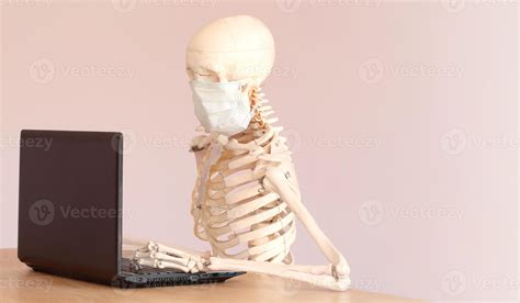Skeleton In A Medical Mask Using A Computer In The Office